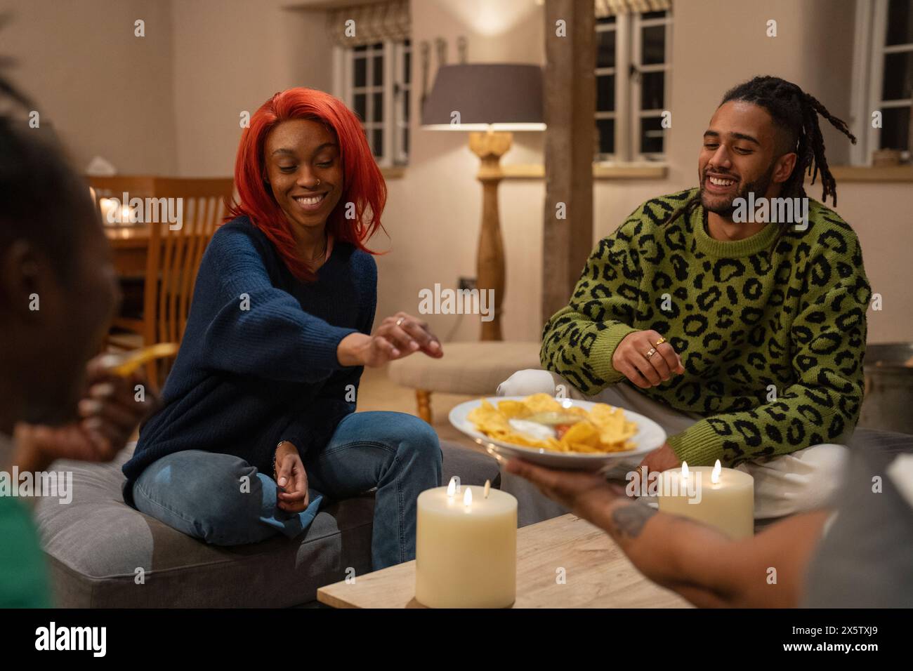 Smiling friends relaxing at home, sharing tortilla chips Stock Photo ...