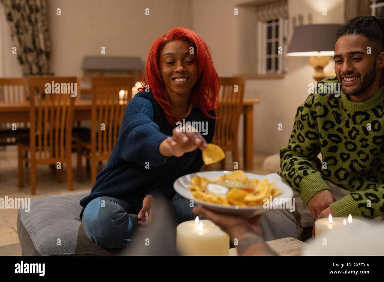 Smiling friends relaxing at home, sharing tortilla chips Stock Photo ...
