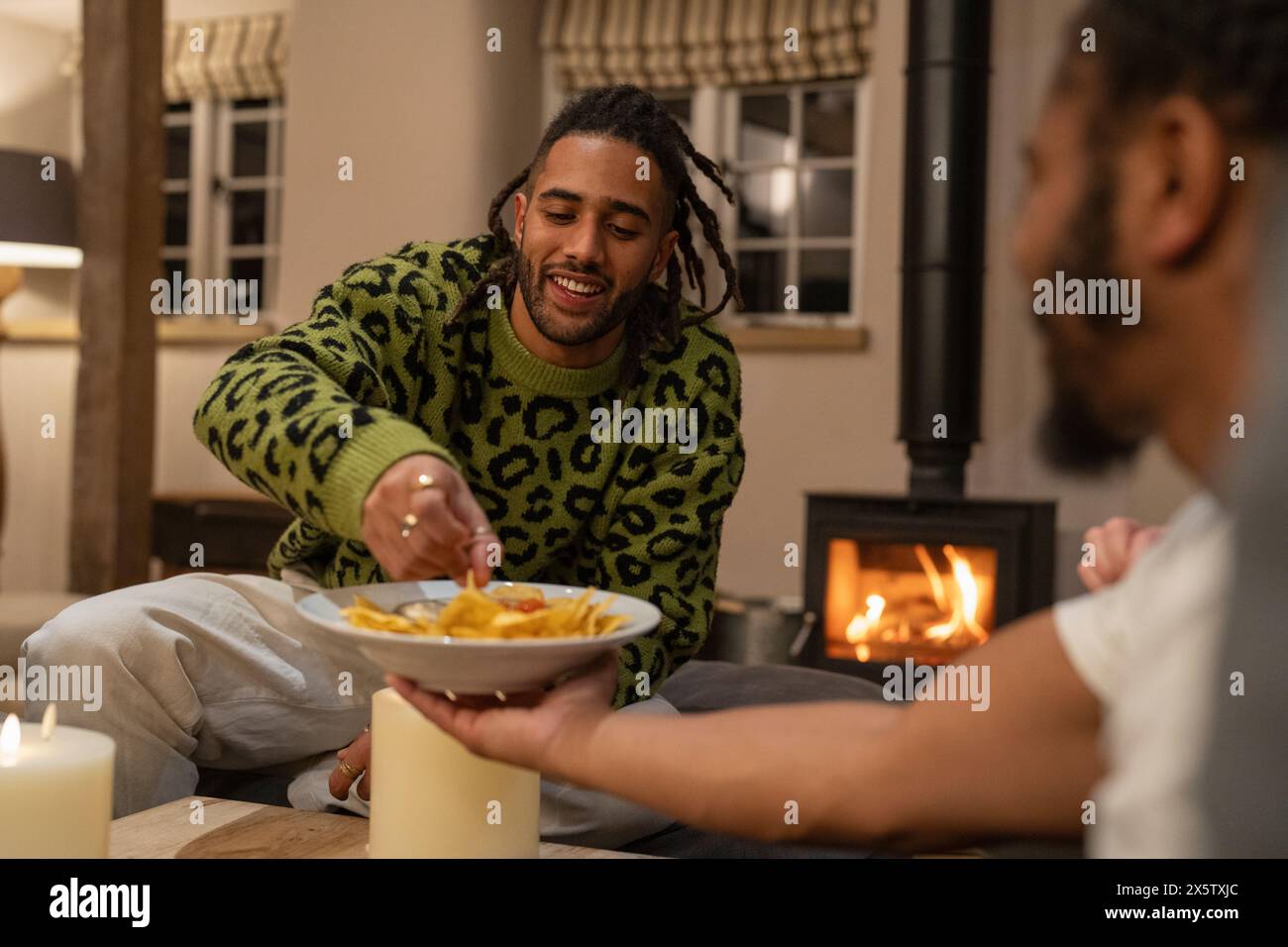 Smiling friends relaxing at home, sharing tortilla chips Stock Photo ...