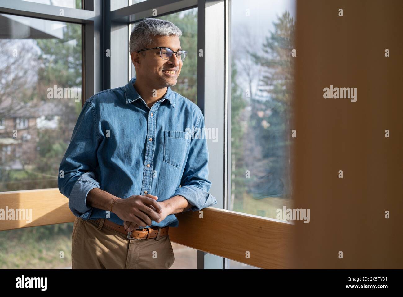 Smiling mature businessman looking through office window Stock Photo ...