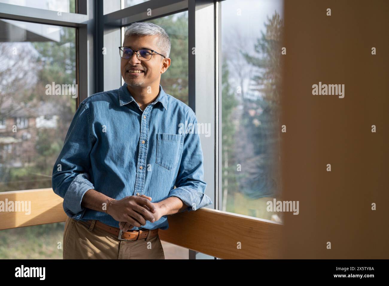 Smiling mature businessman looking through office window Stock Photo ...