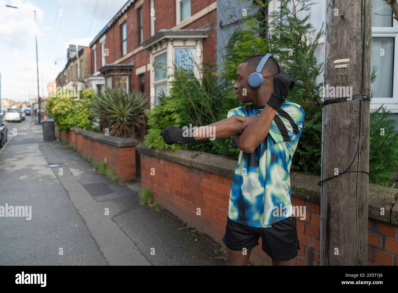Athlete with headphones stretching arm on sidewalk Stock Photo - Alamy