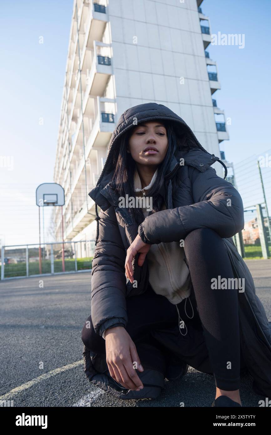 Portrait of woman in overcoat with hood crouching on basketball court ...