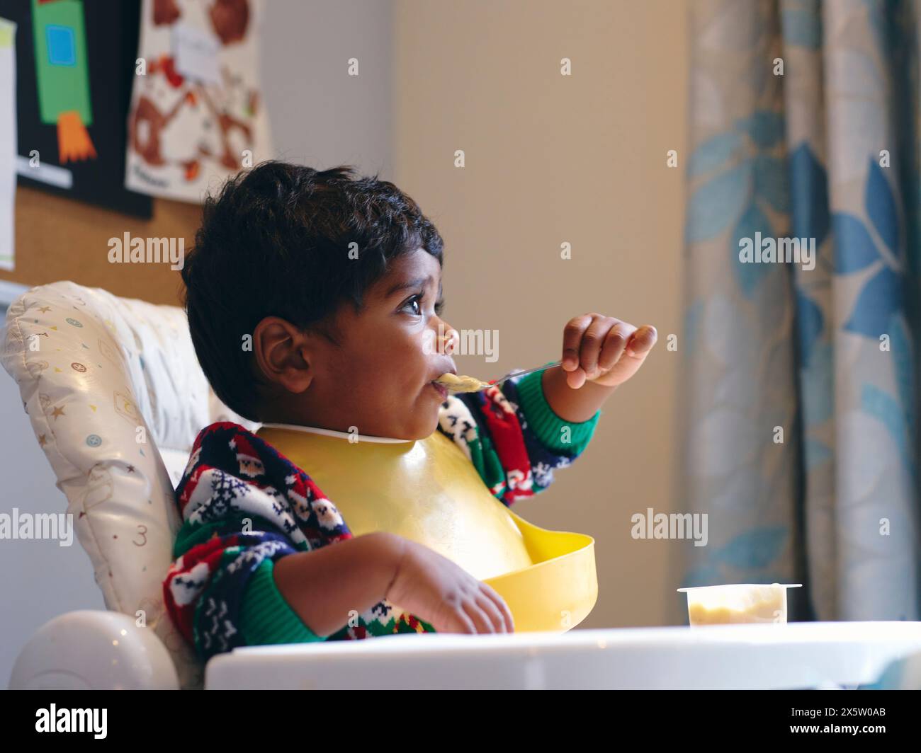 Boy sitting in high chair and eating Stock Photo - Alamy