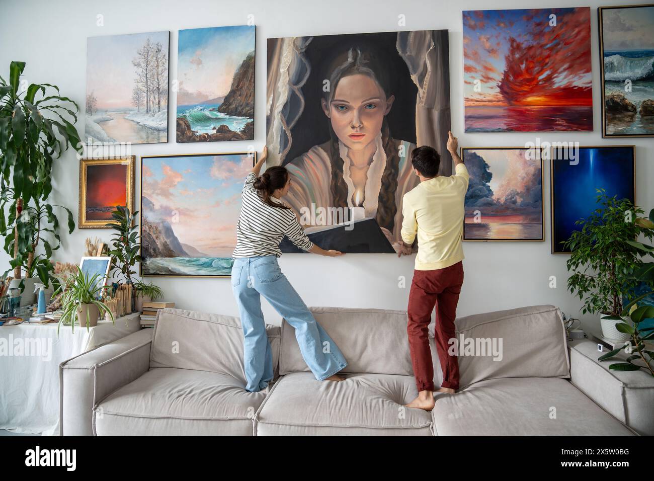 Painters couple at home studio hang artwork on wall. Guy girl together make picture composition ...