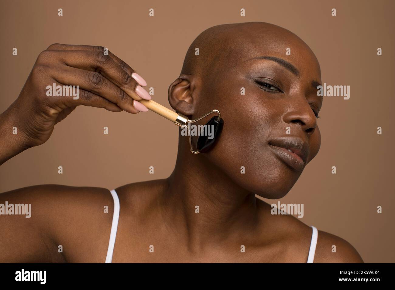Studio portrait of woman massaging face with stone roller Stock Photo ...