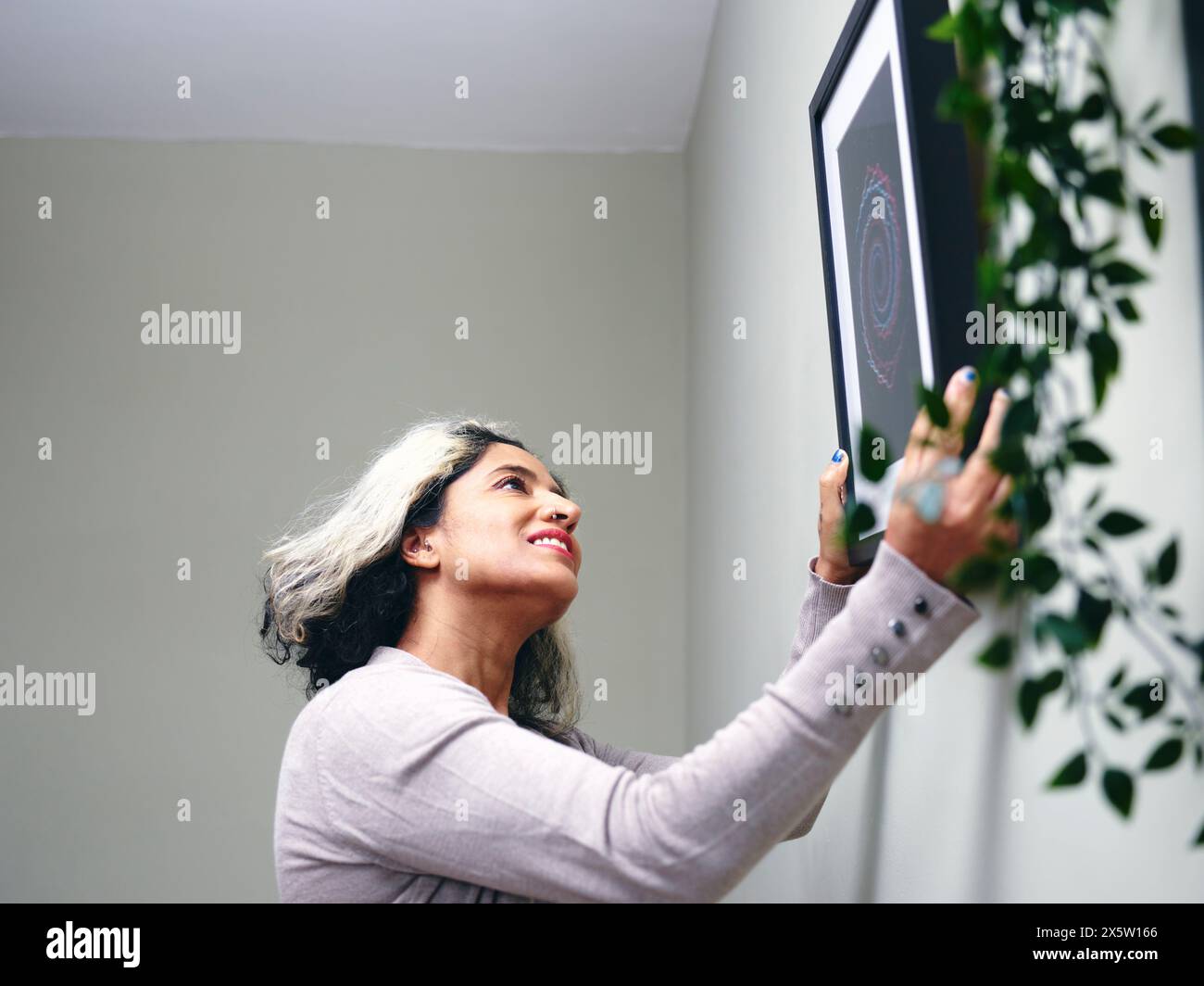 Woman hanging picture on wall Stock Photo - Alamy