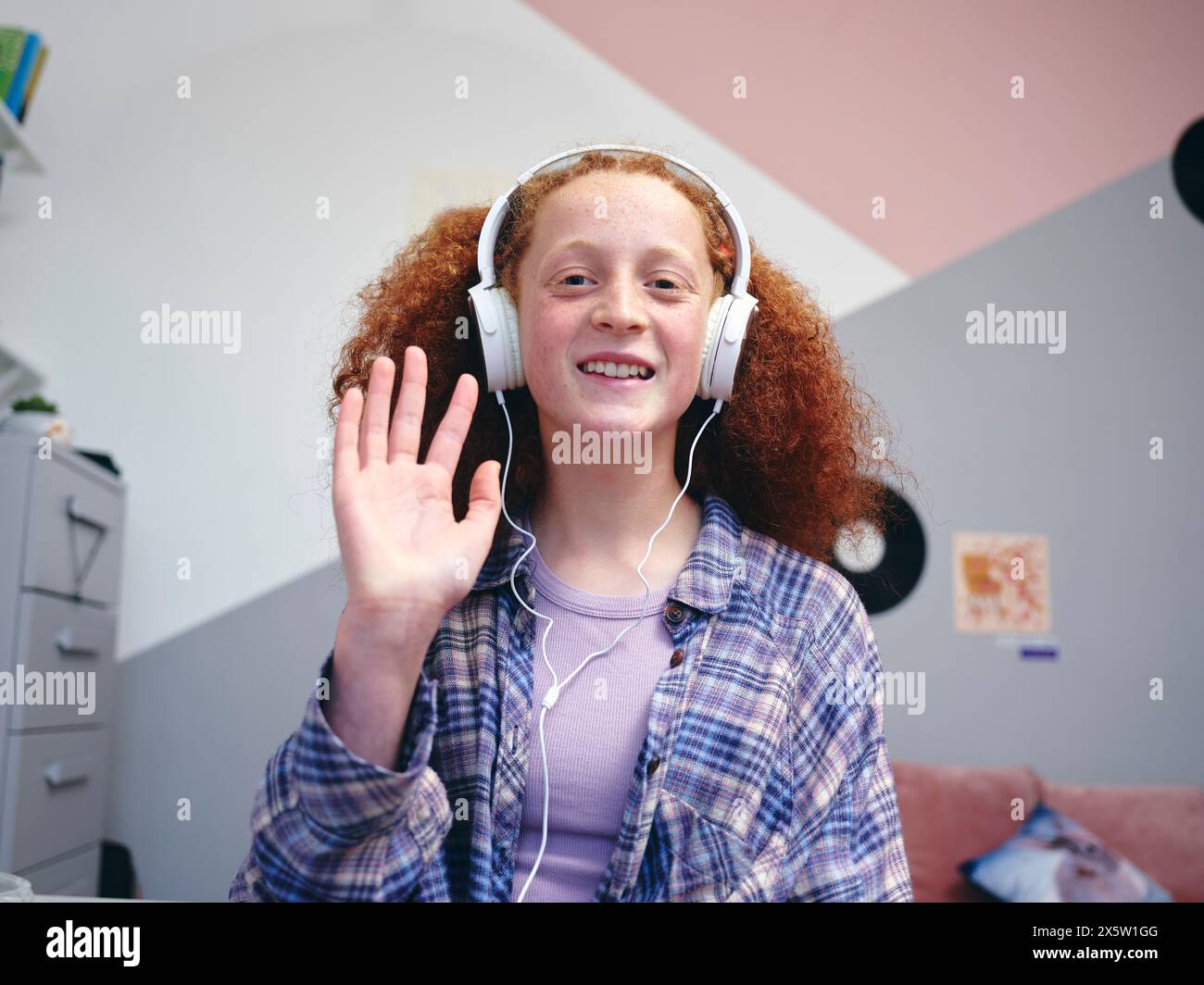 Girl wearing headphones waving to camera Stock Photo - Alamy
