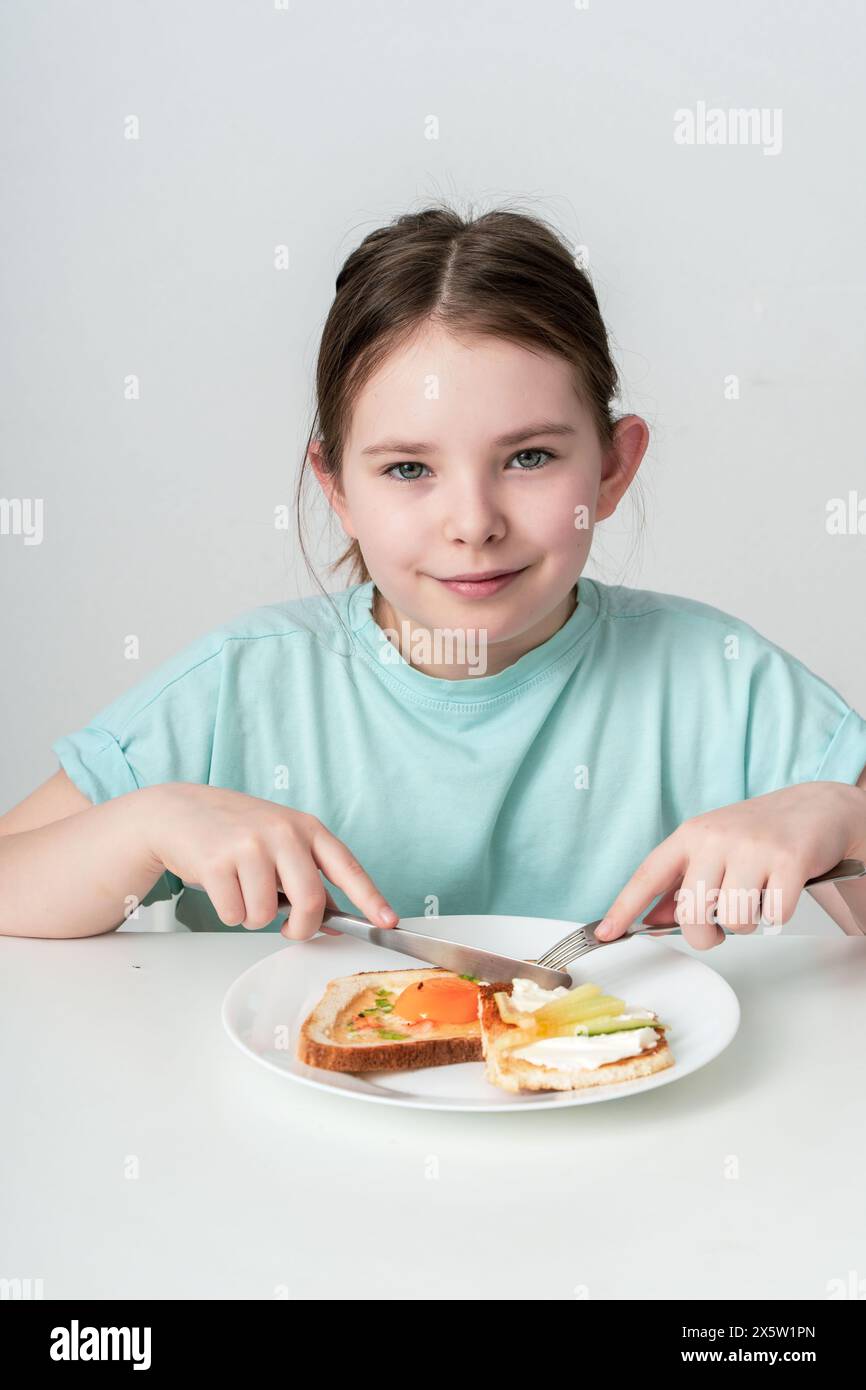 Cute little girl eating fried egg with toast and vegetables. The ...