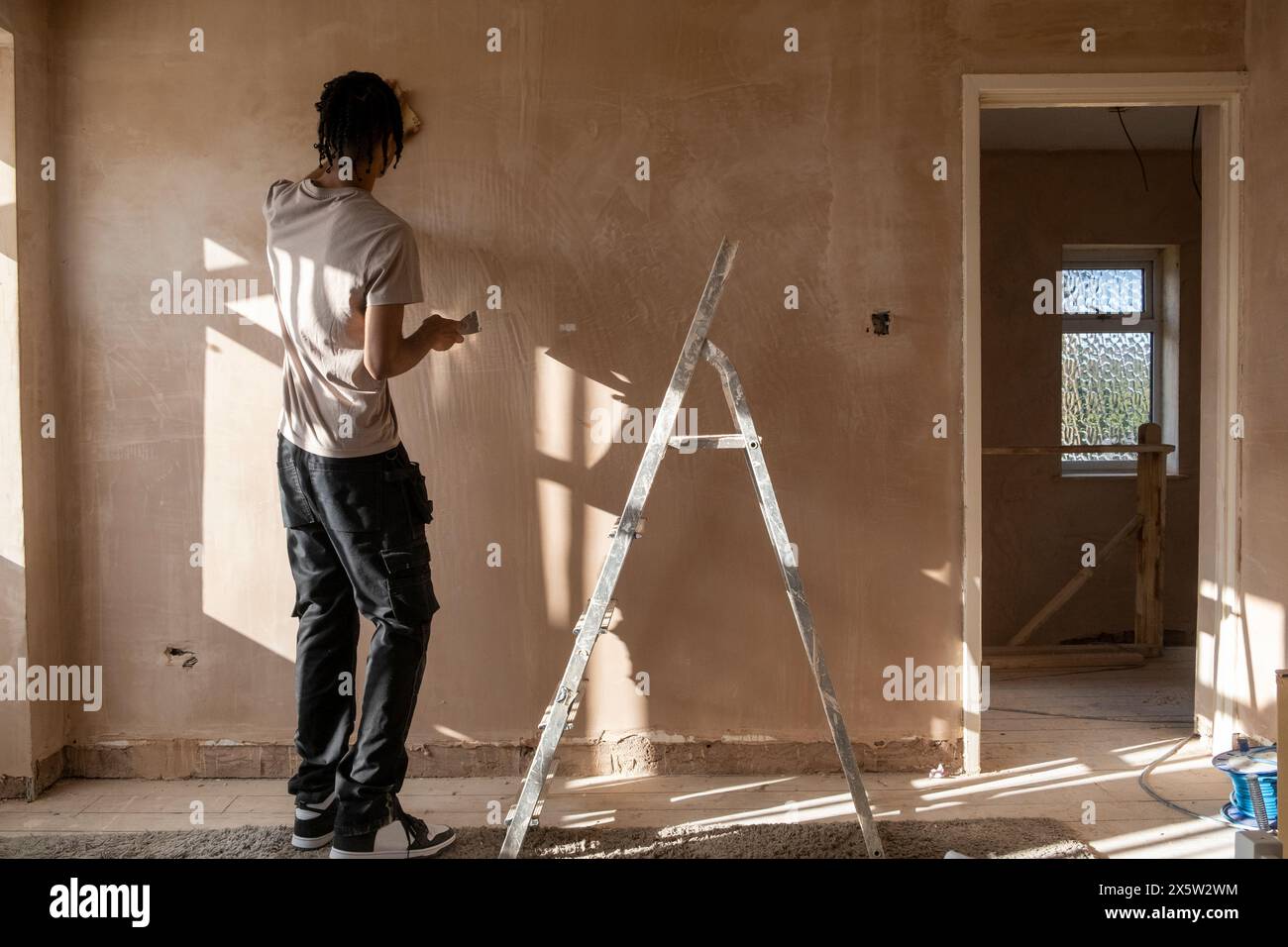 Rear view of teenage boy sanding wall in house Stock Photo - Alamy