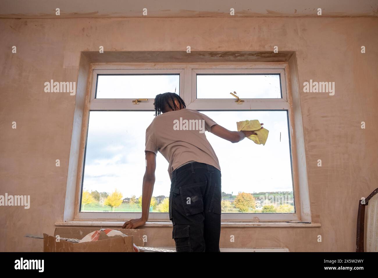 Rear view of teenage boy washing window in house under renovation Stock ...