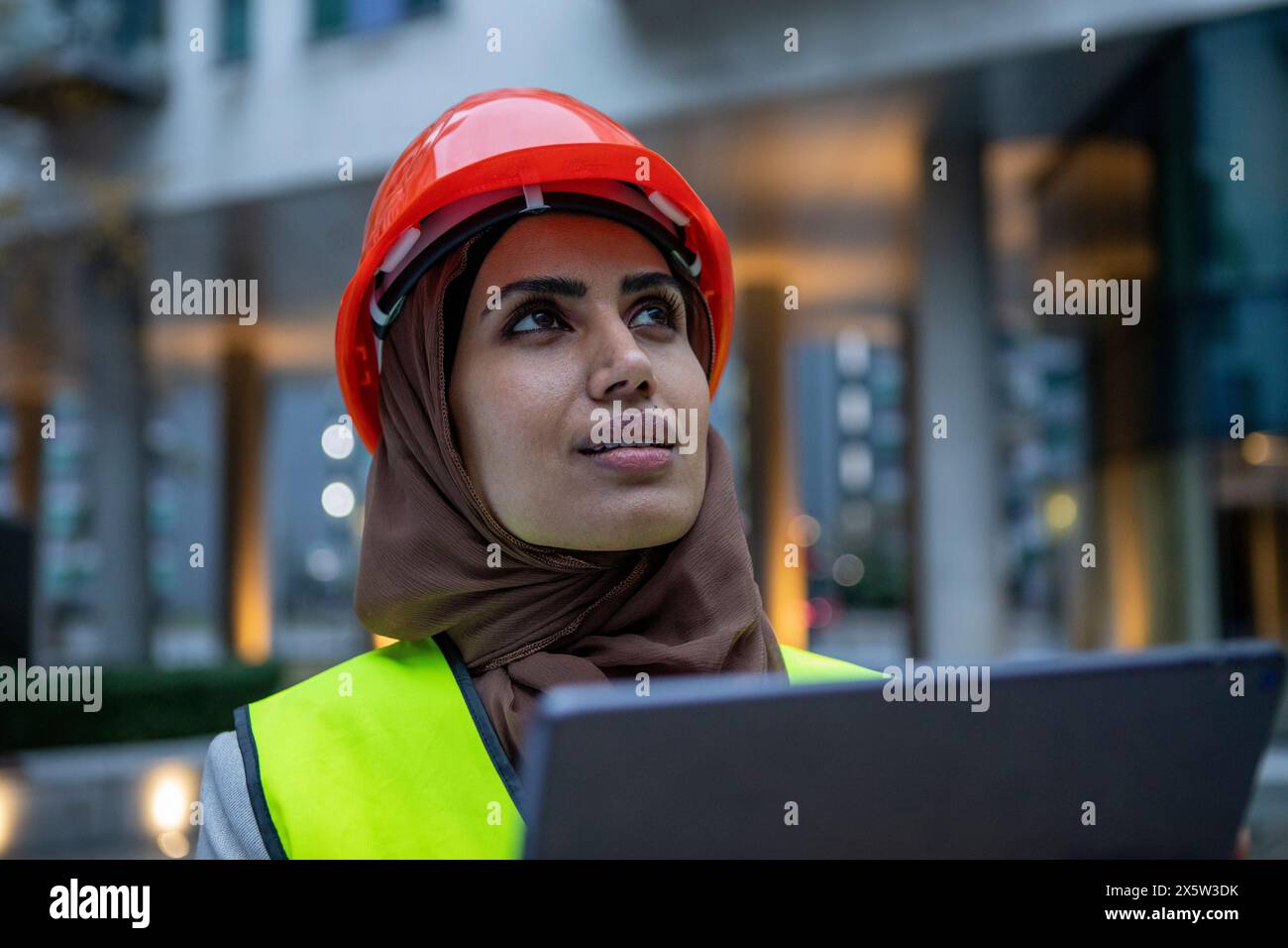 UK, London, Female engineer in hijab and hardhat using digital tablet ...