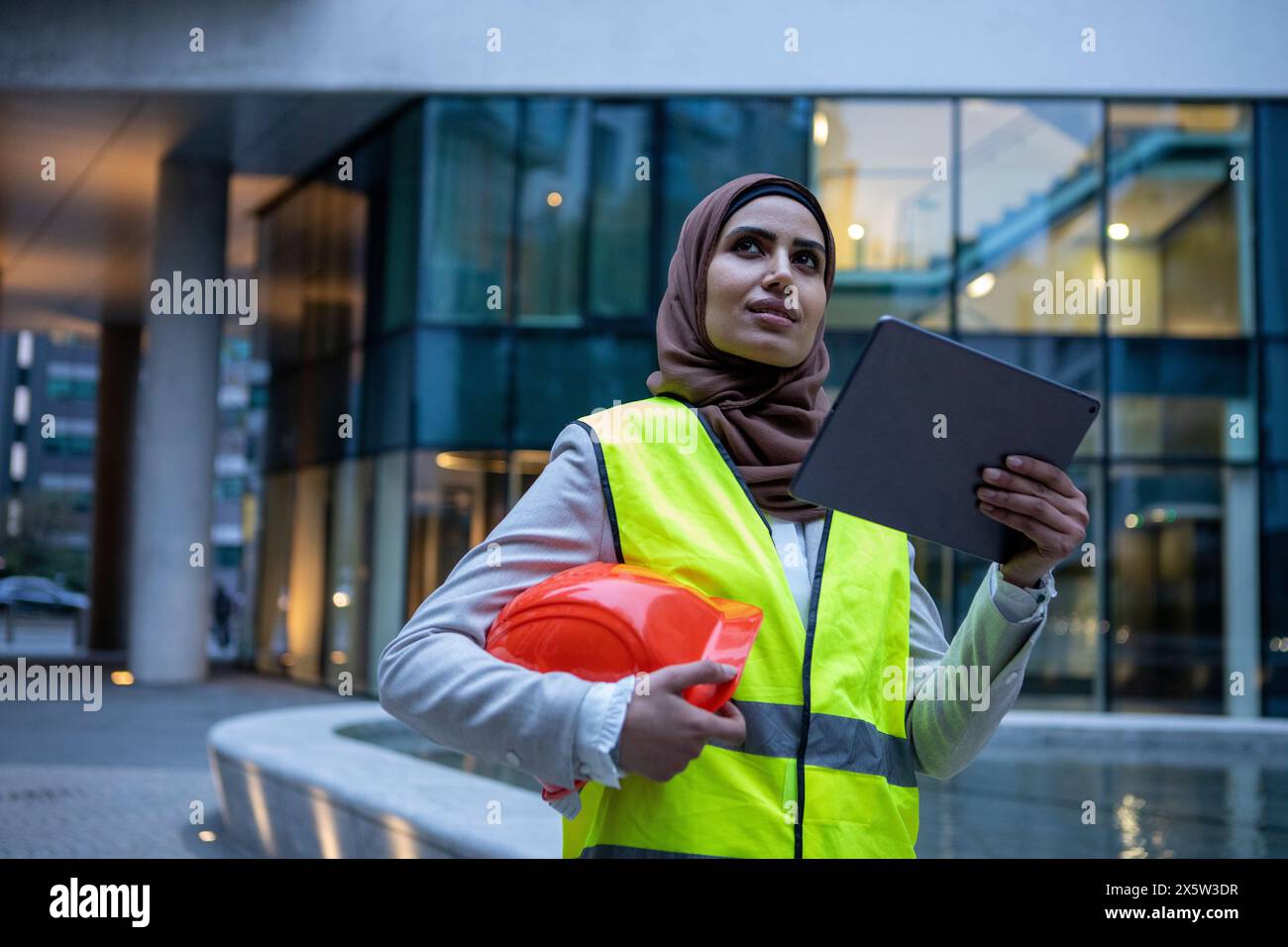UK, London, Female engineer in hijab holding tablet on front of modern ...