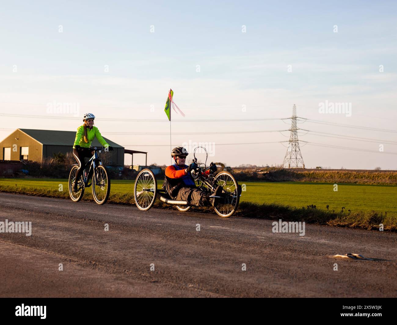 Woman riding bike and disabled man riding handcycle on country road ...