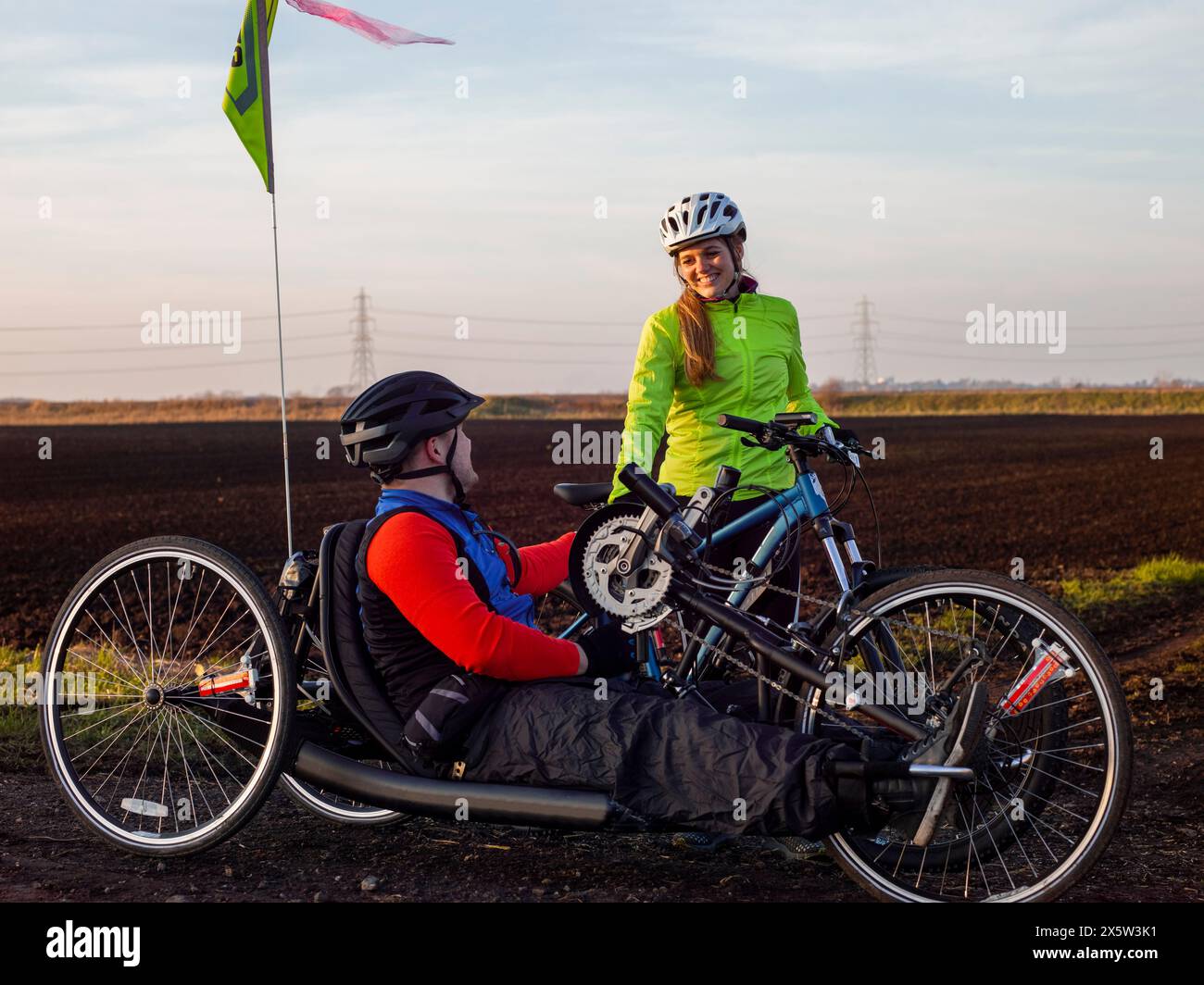 Disabled man on handcycle and woman with bicycle in rural landscape ...