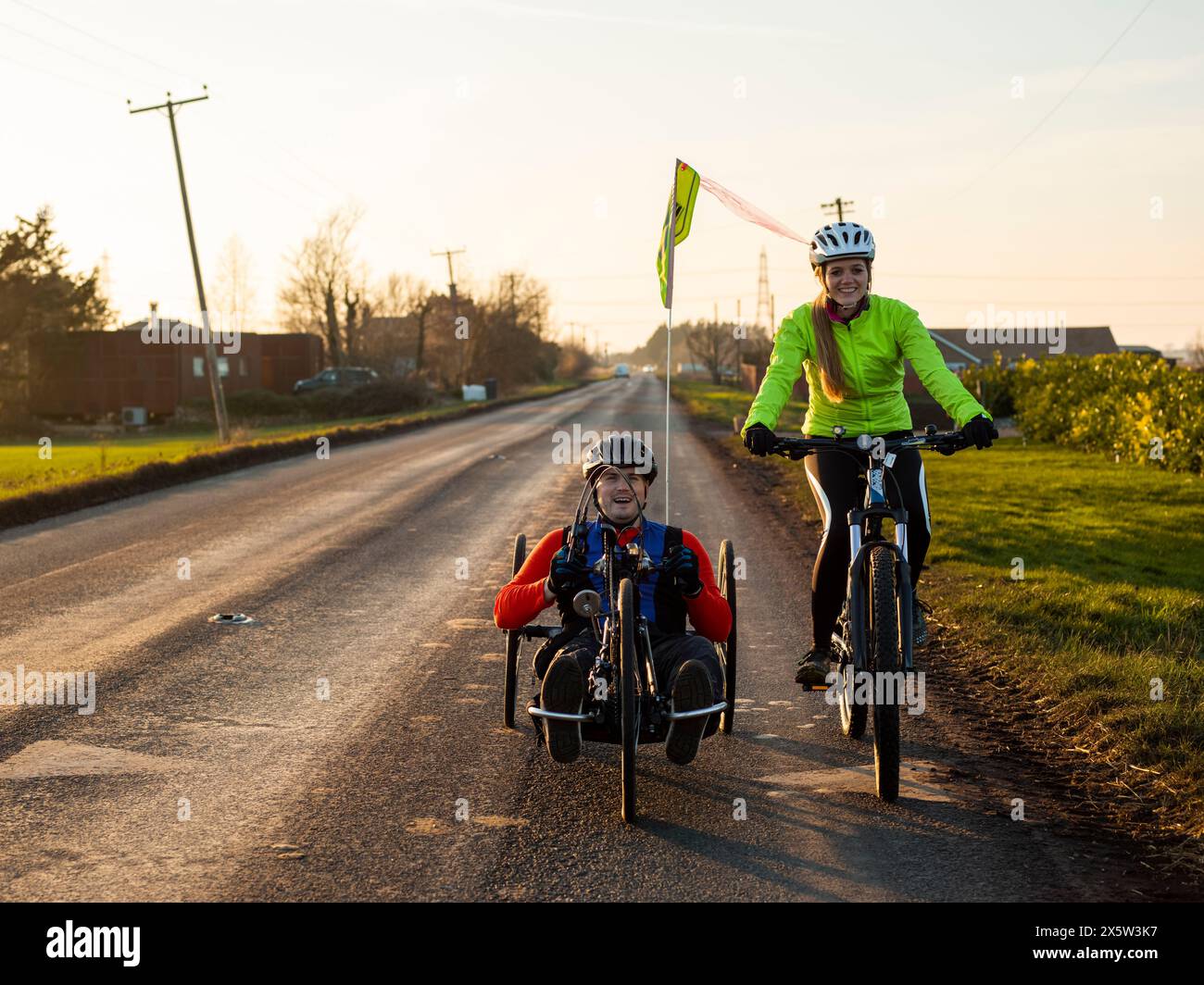 Woman riding bike and disabled man riding handcycle on country road ...