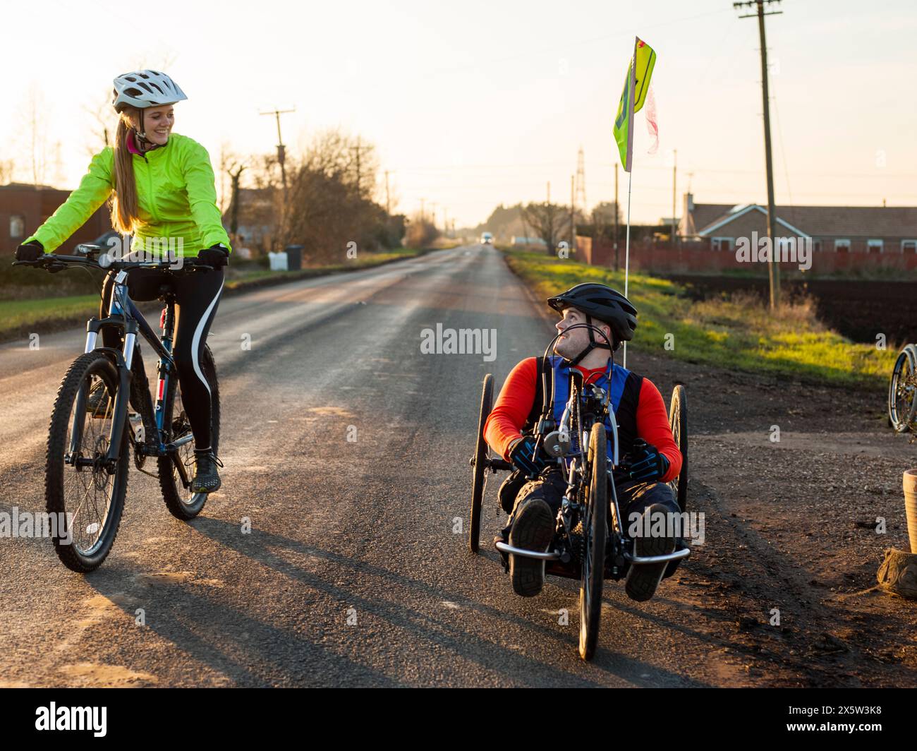Woman riding bike and disabled man riding handcycle on country road ...