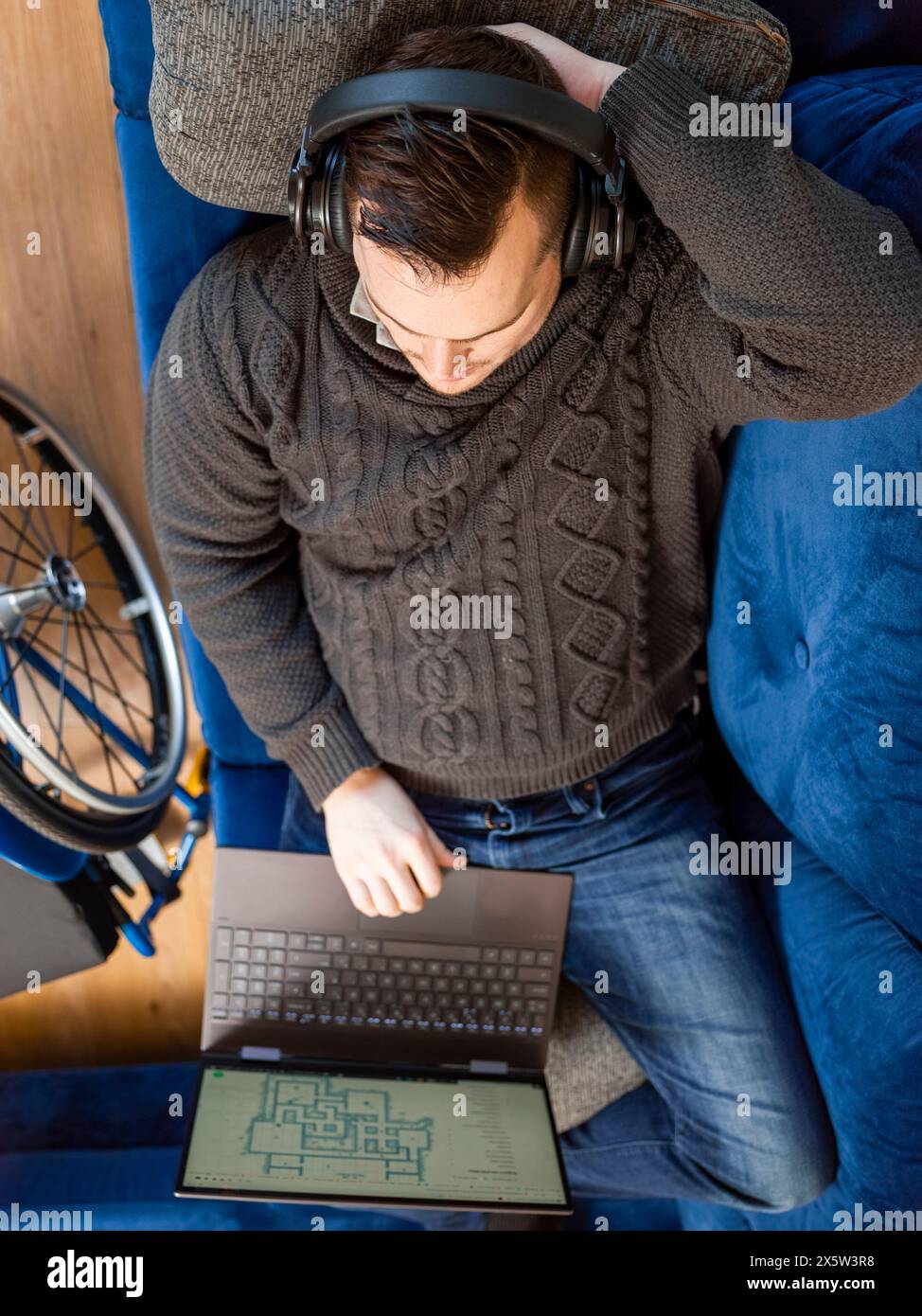 Overhead view of man with headphones and laptop on sofa next to ...