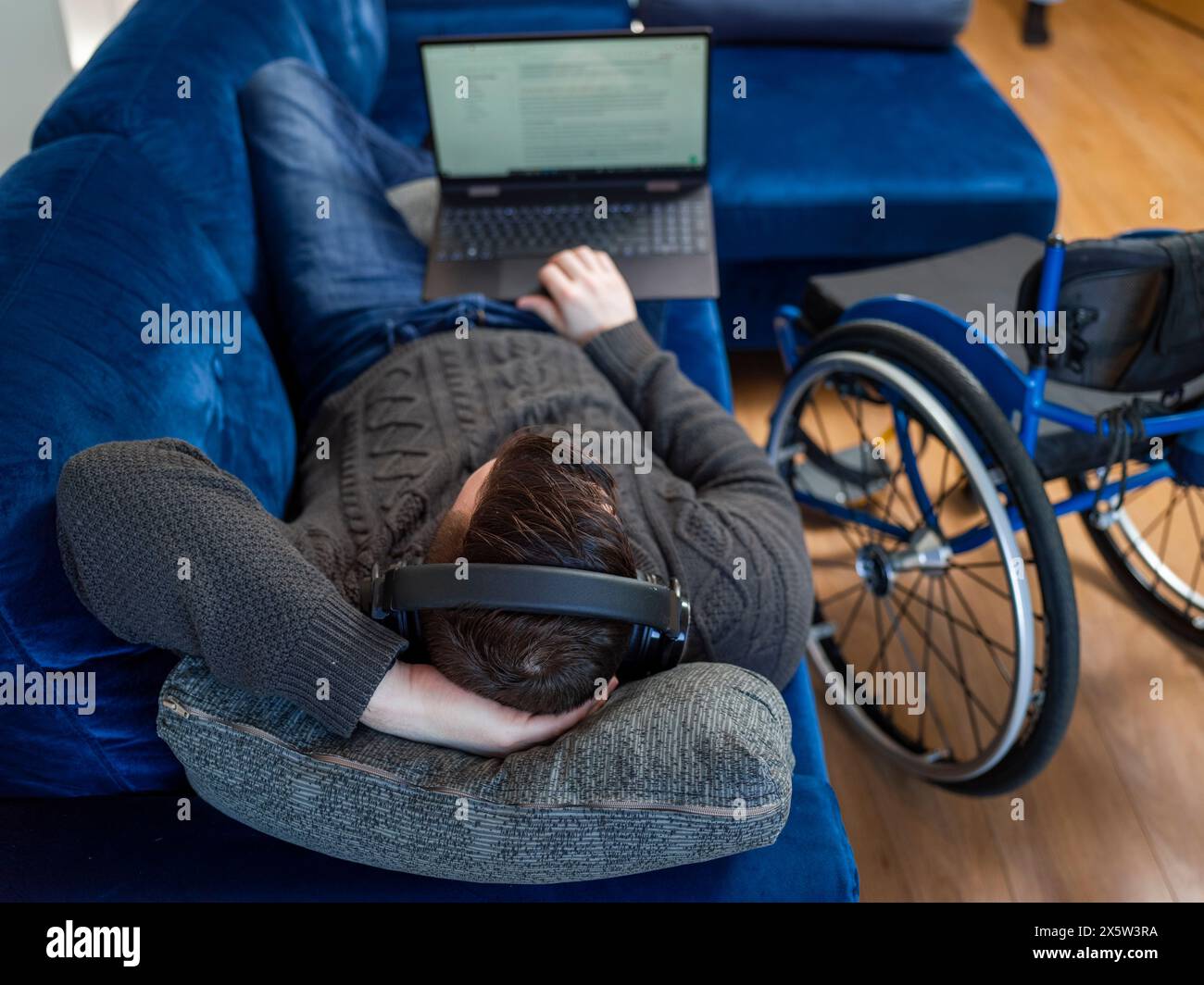 Overhead view of man with headphones and laptop on sofa next to ...