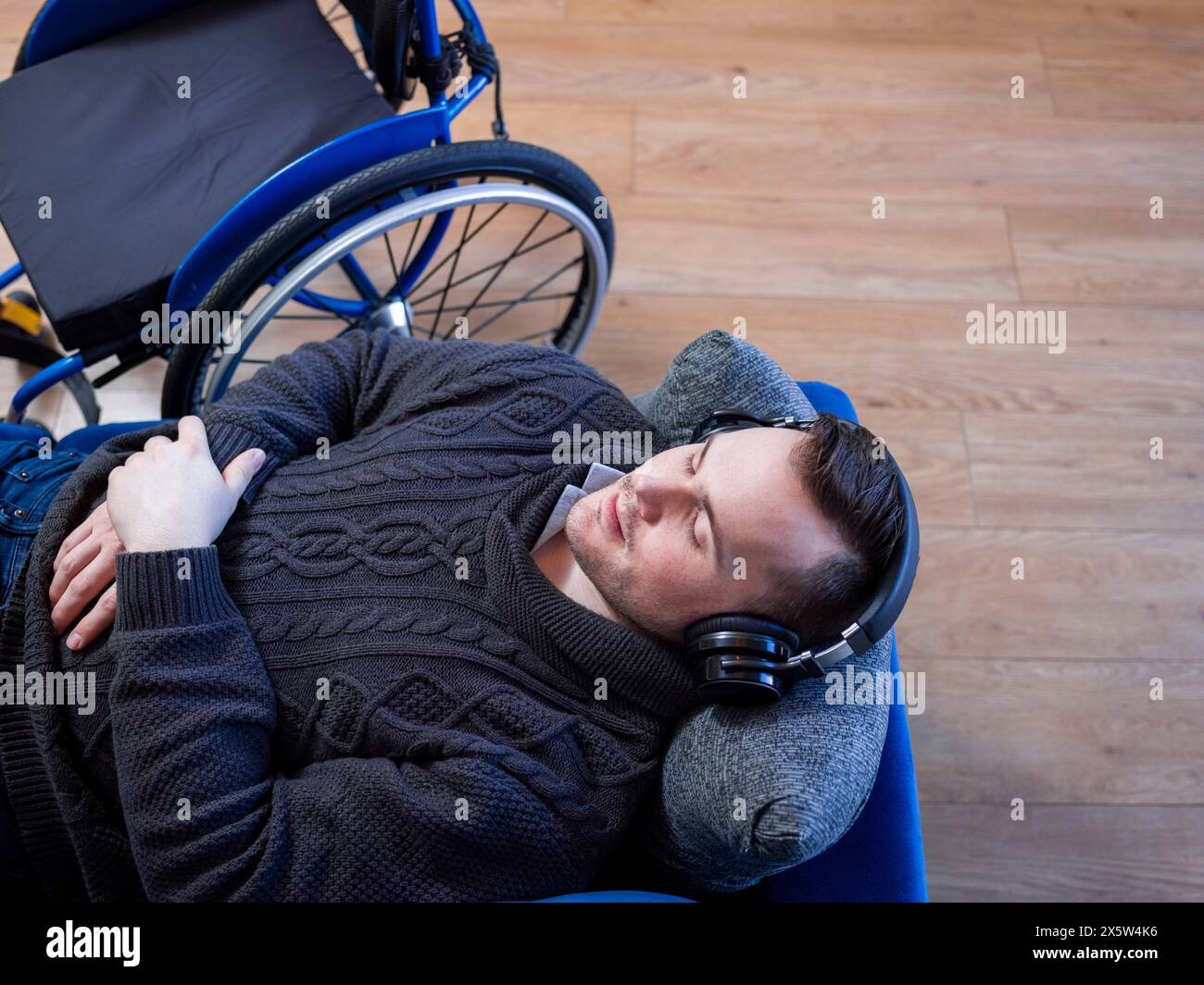Overhead view of man with headphones on sofa next to wheelchair Stock ...