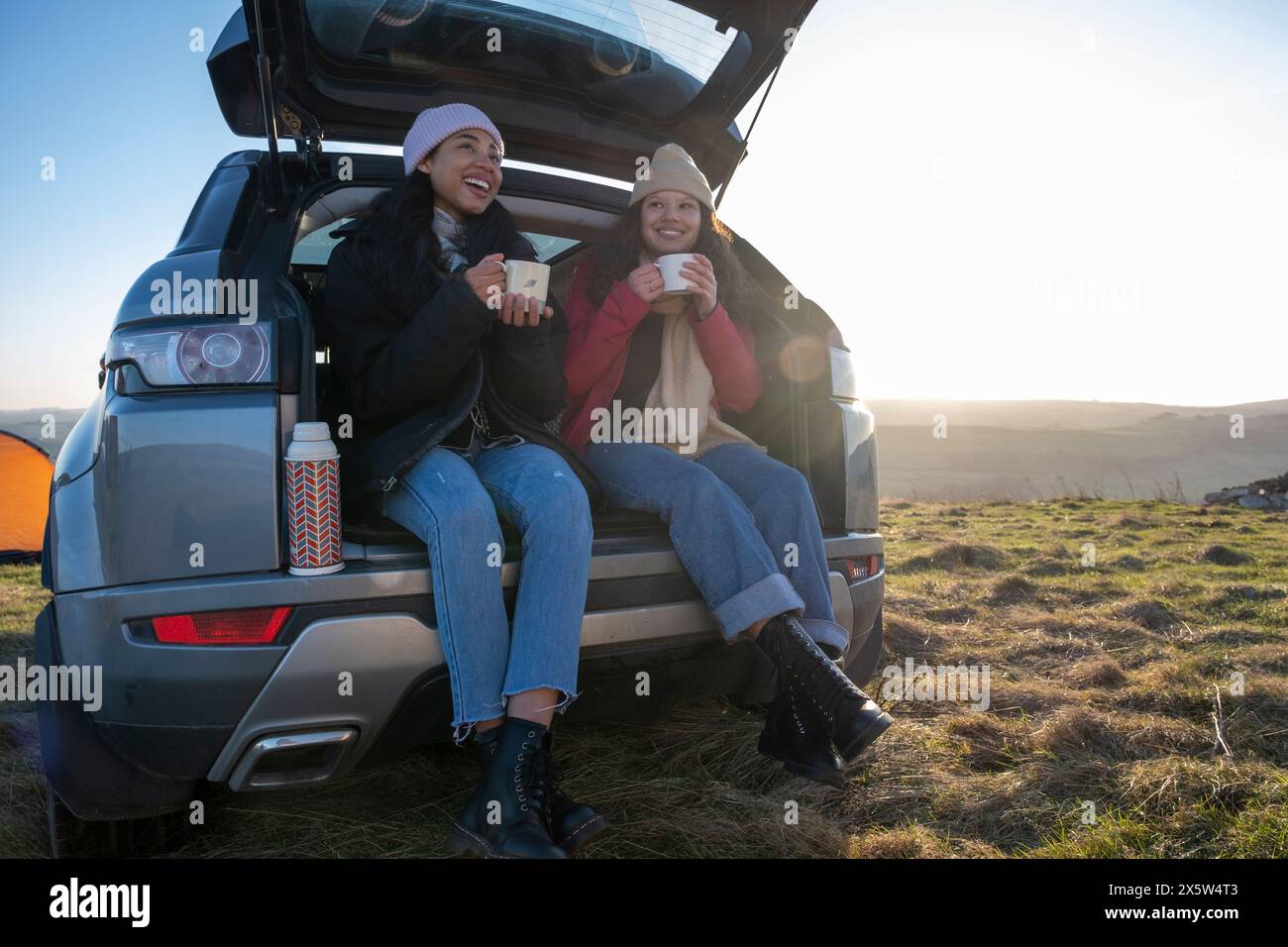 Female friends sitting in car trunk and drinking tea Stock Photo - Alamy