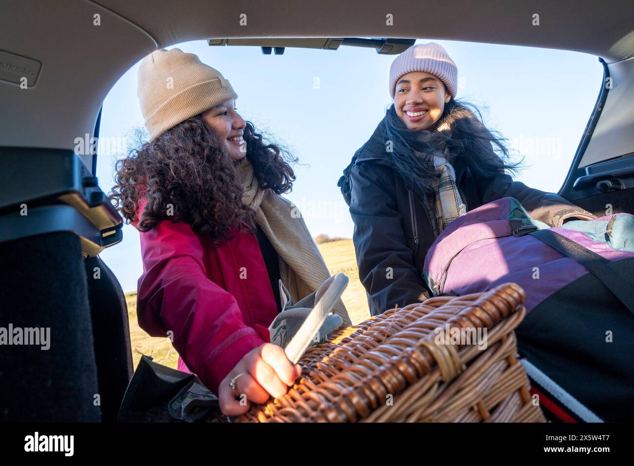 Female friends grabbing bags from car trunk Stock Photo - Alamy