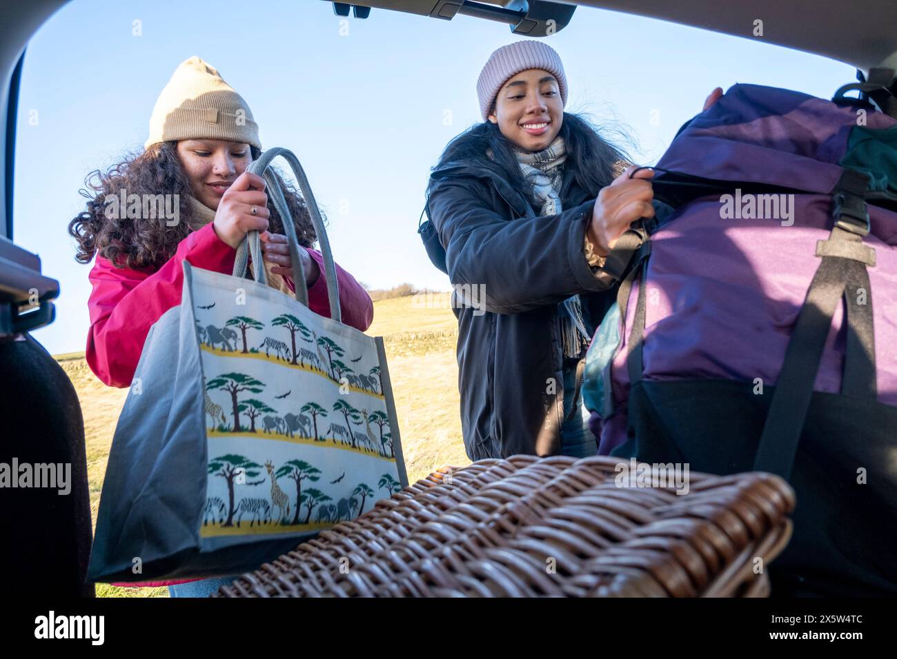 Female friends grabbing bags from car trunk Stock Photo - Alamy