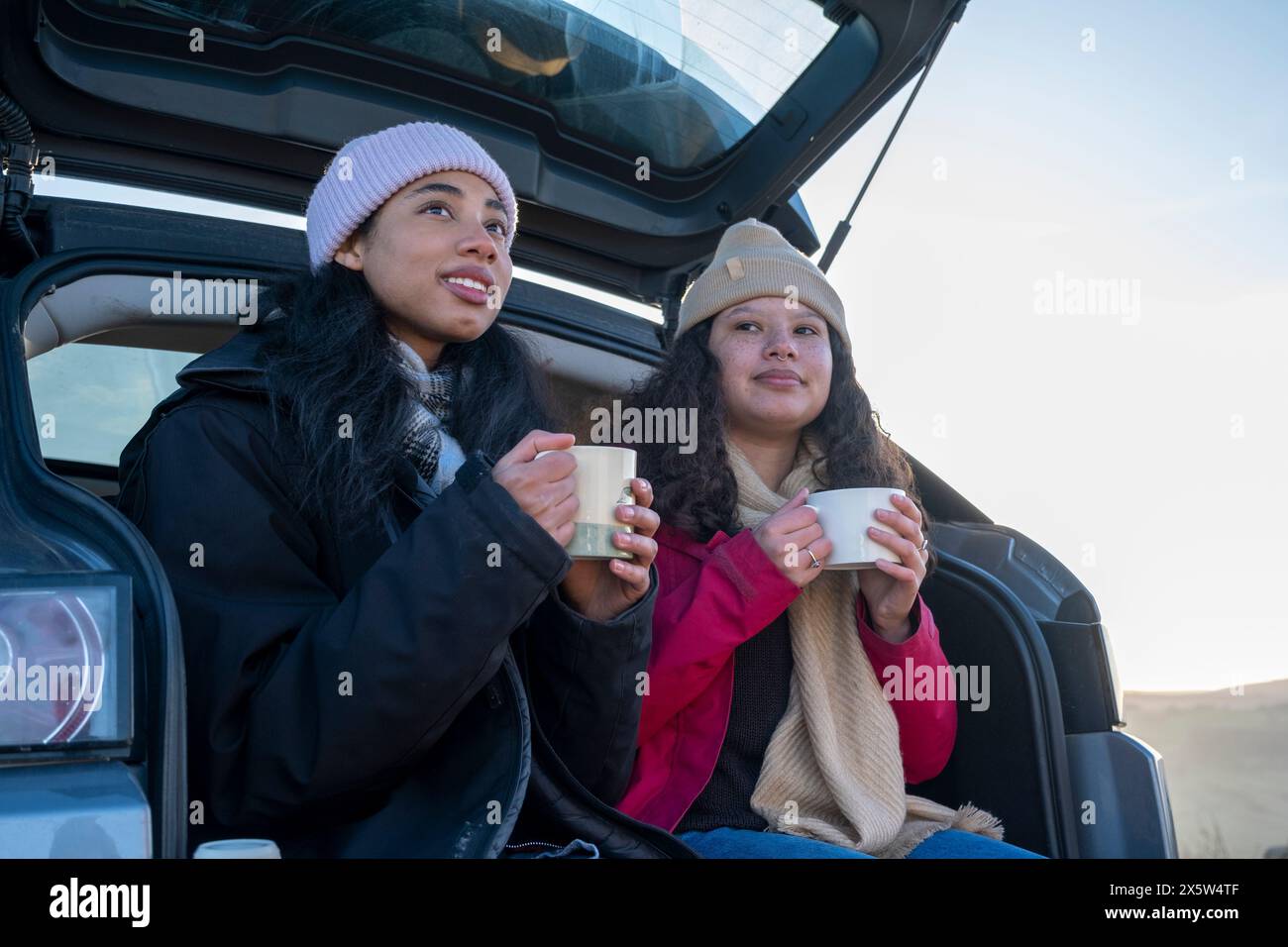 Female friends sitting in car trunk and drinking tea Stock Photo - Alamy