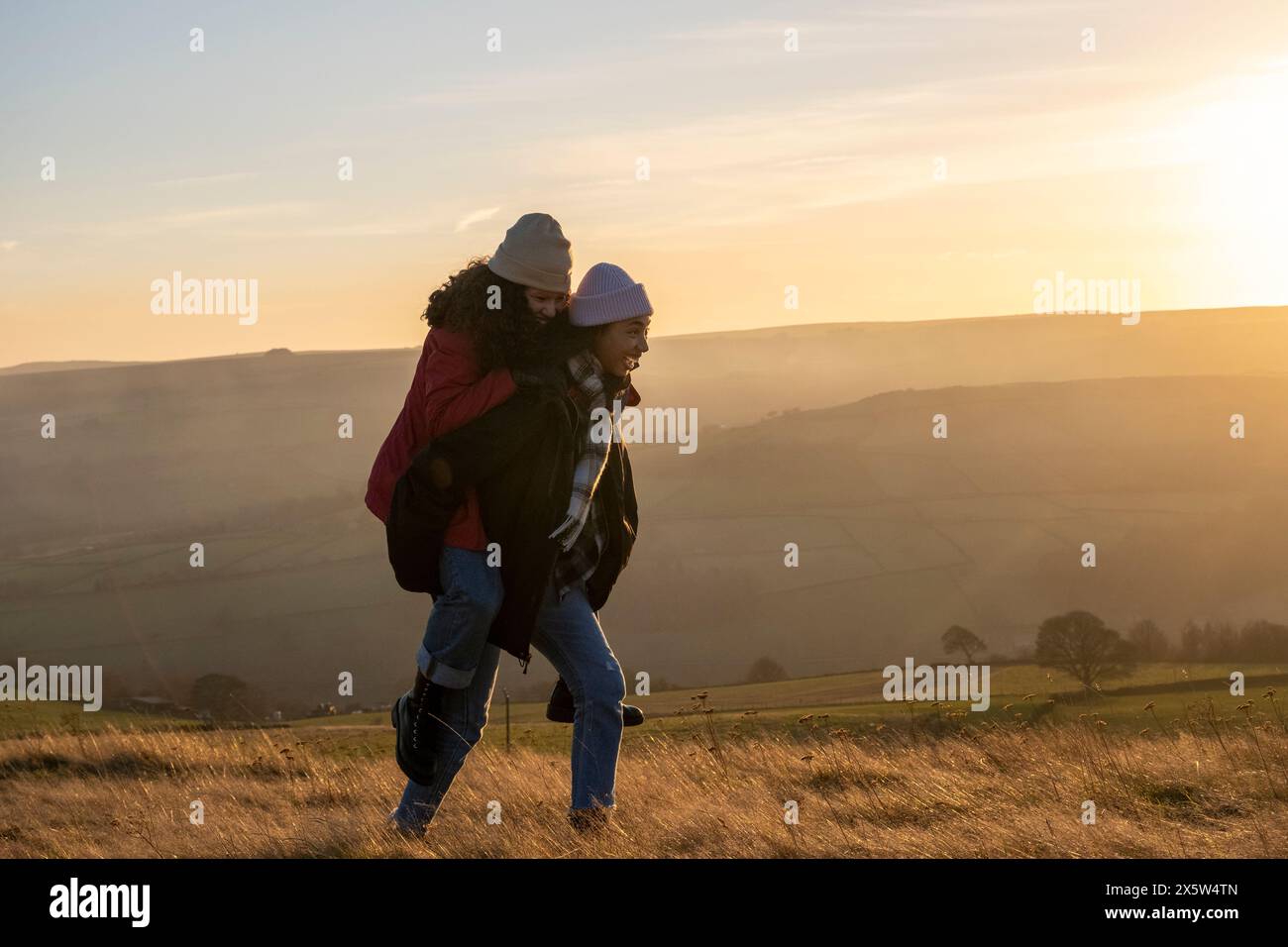 Young woman giving friend piggyback ride in rural landscape Stock Photo ...