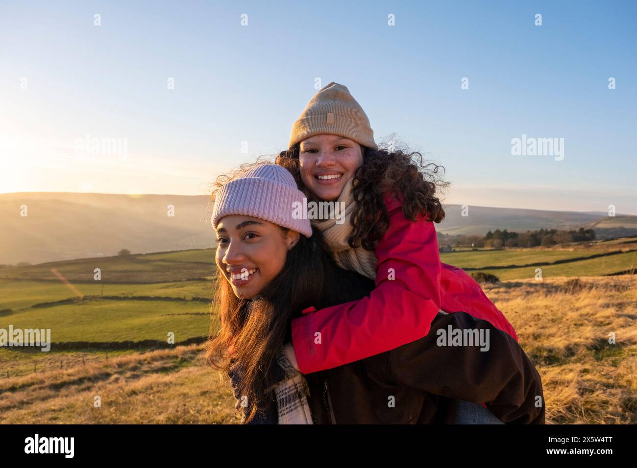 Young woman giving friend piggyback ride in rural landscape Stock Photo ...