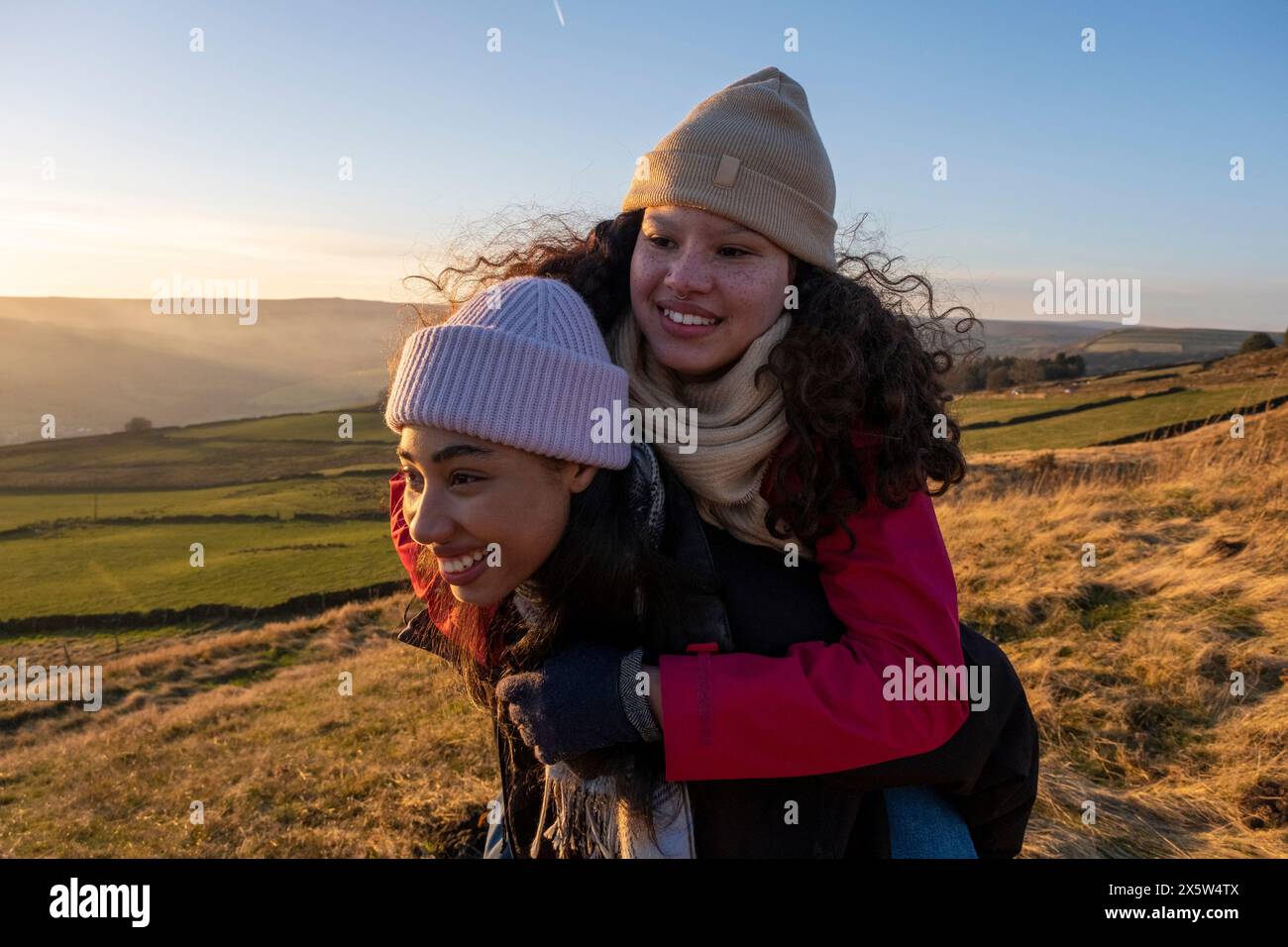 Young woman giving friend piggyback ride in rural landscape Stock Photo ...