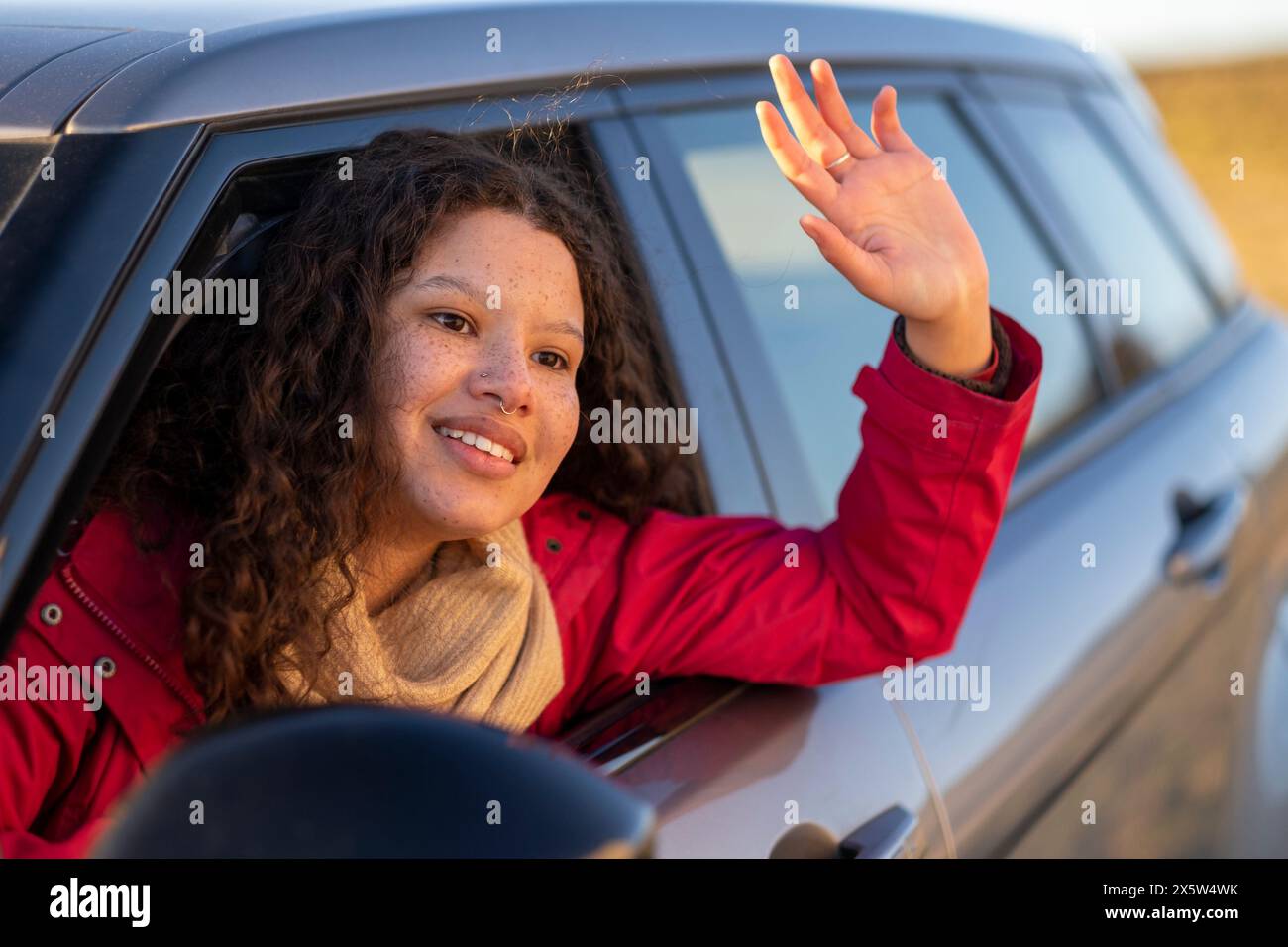 Young woman waving out of car window Stock Photo - Alamy