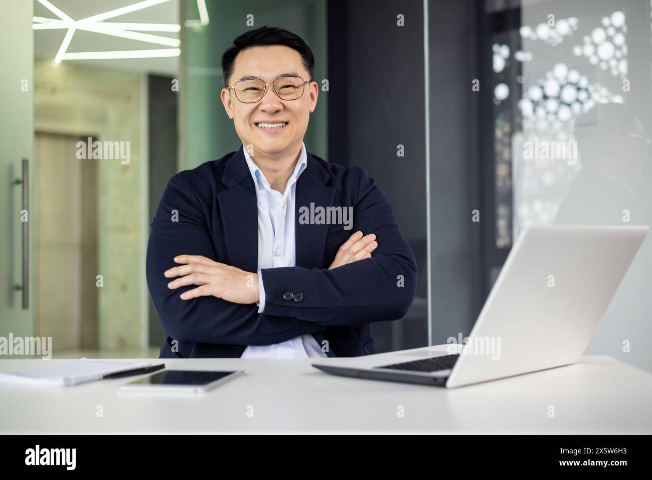 A cheerful Asian male executive stands confidently at his desk in a ...