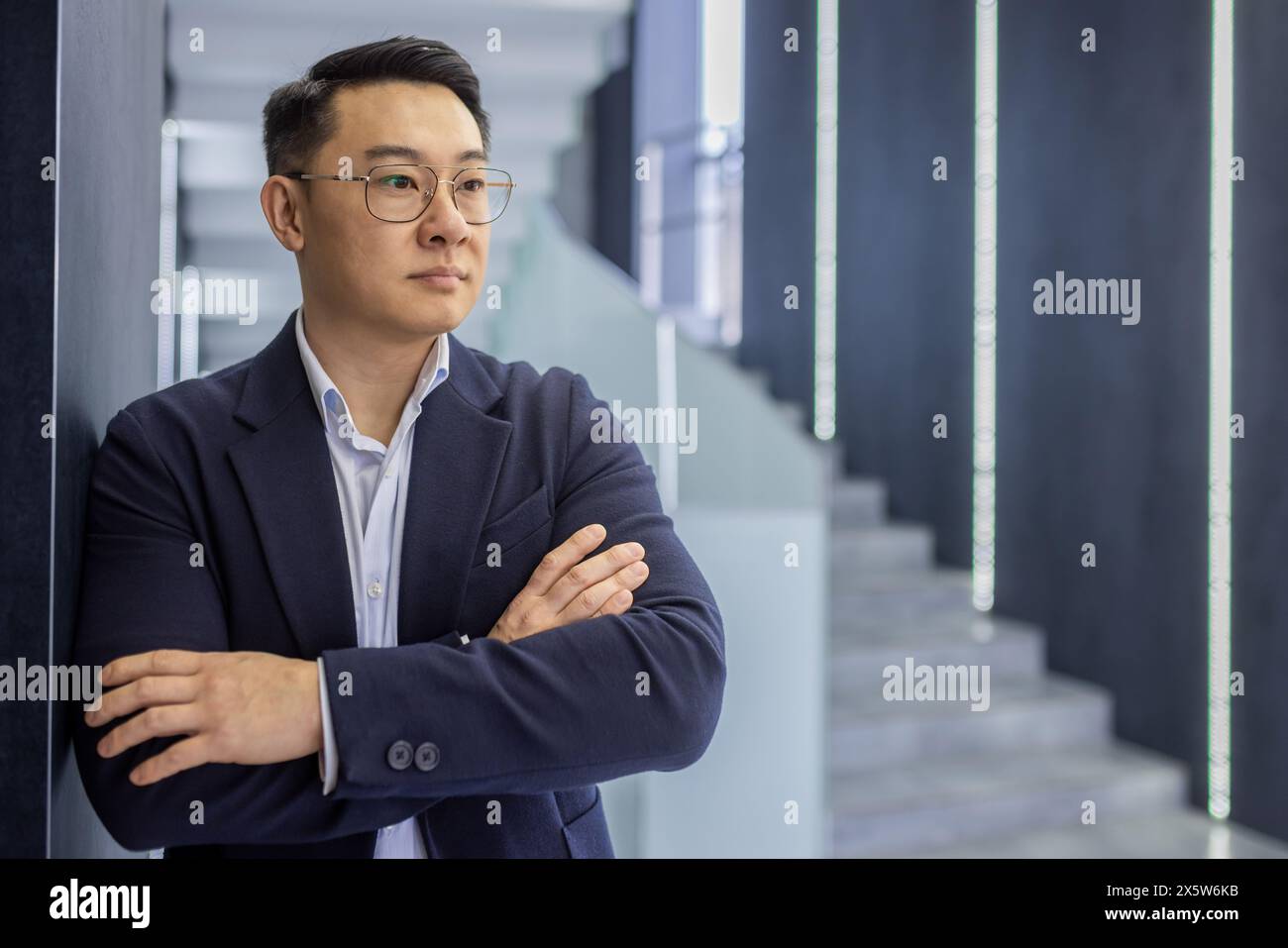 A thoughtful and confident Asian businessman with arms crossed ...