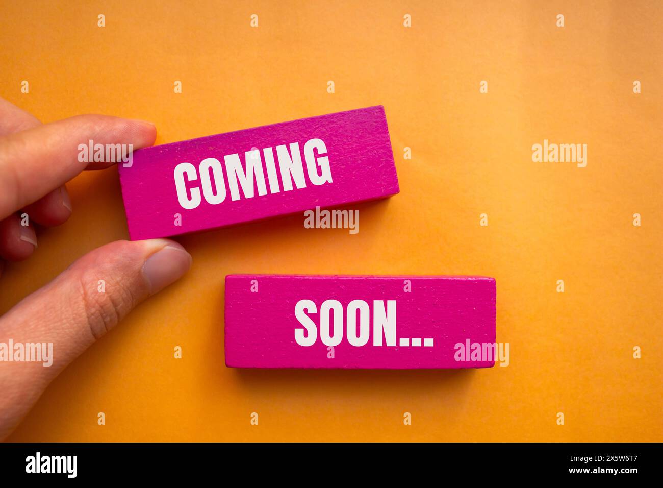 Coming soon words written on pink wooden blocks with orange background ...