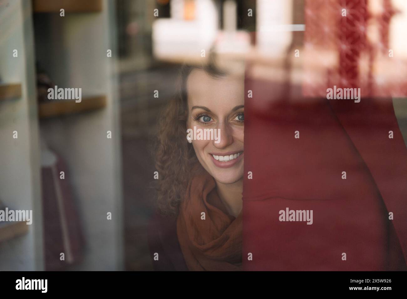 Captivating smile of a young woman with curly hair seen through a cafe ...