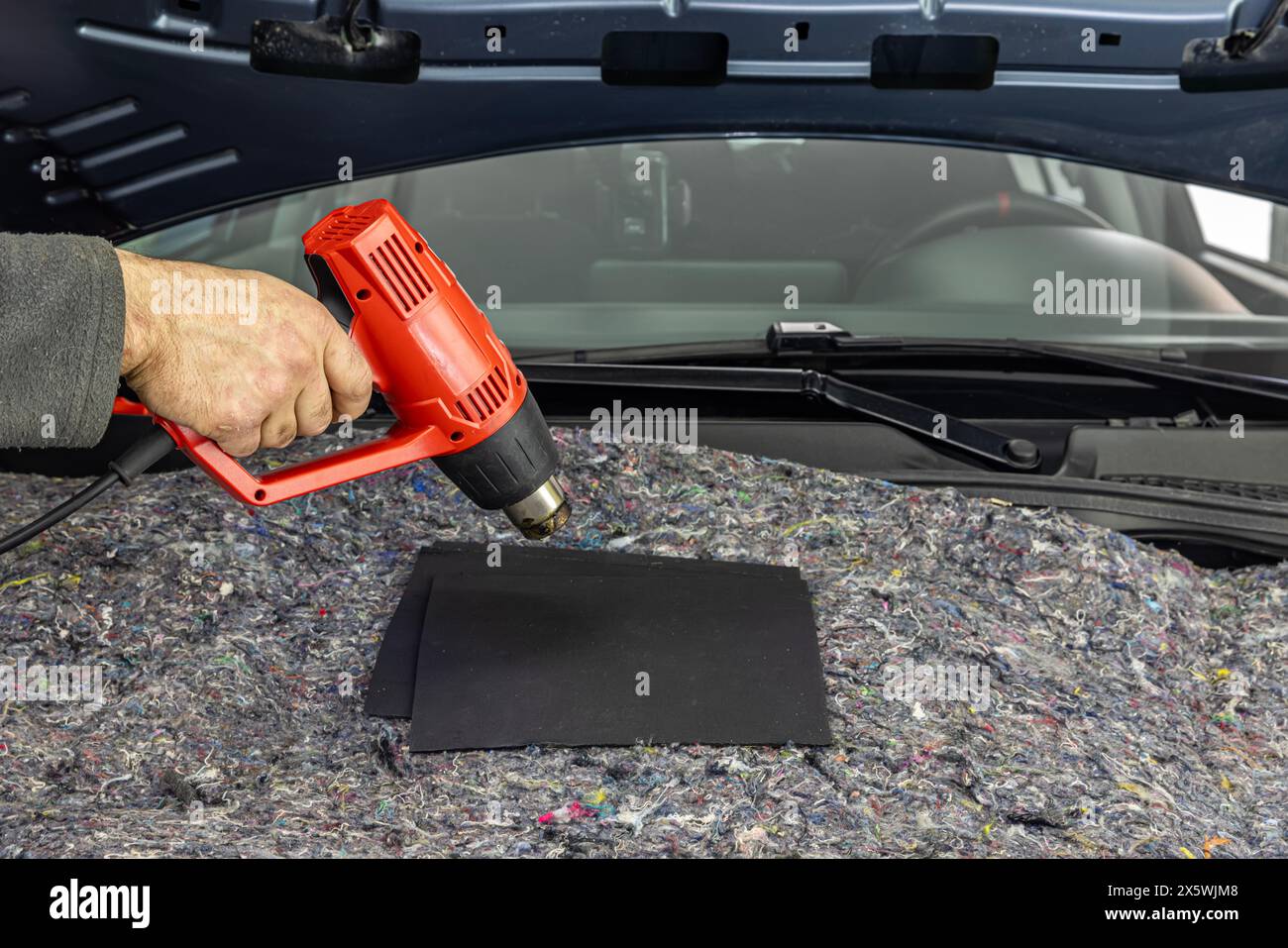 Auto service worker applies soundproof bitumen material to the hood of ...