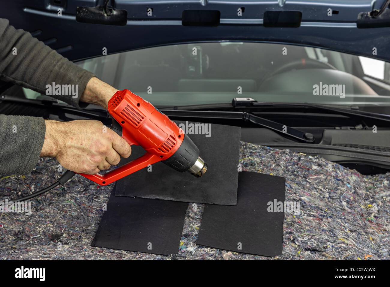 Auto service worker applies soundproof bitumen material to the hood of ...