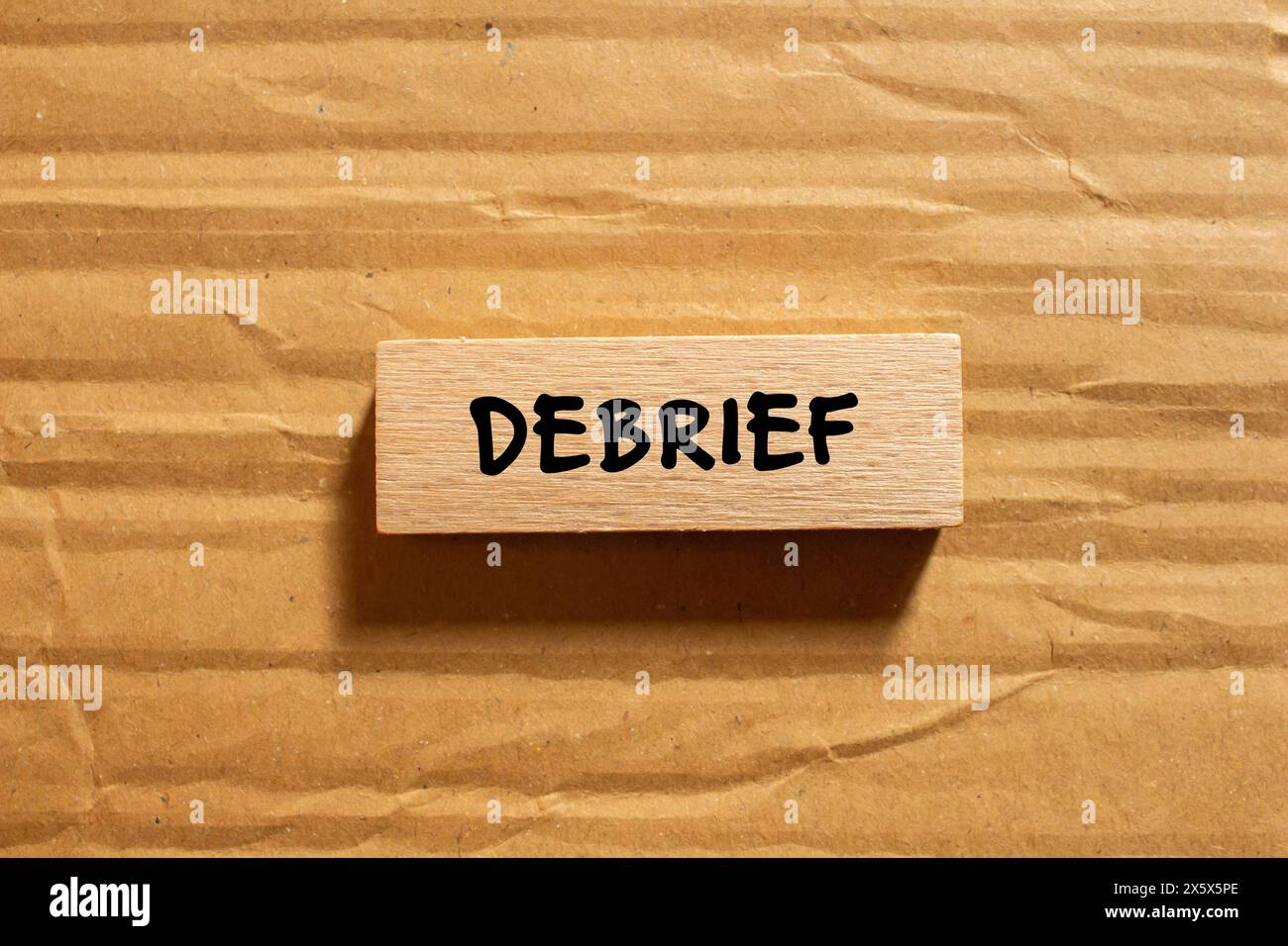 Debrief word written on wooden block with cardboard background ...
