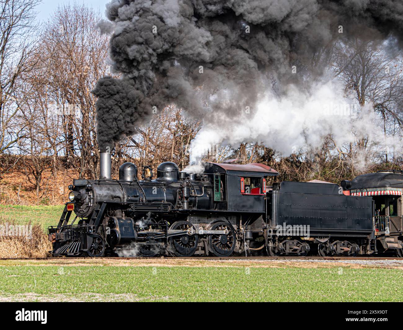A steam train is traveling down the tracks, leaving a trail of smoke ...
