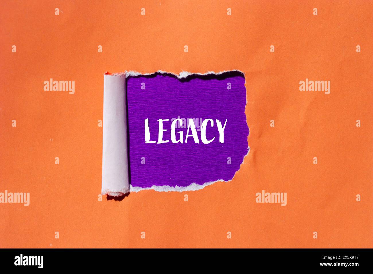 Legacy word written on ripped orange paper with purple background ...