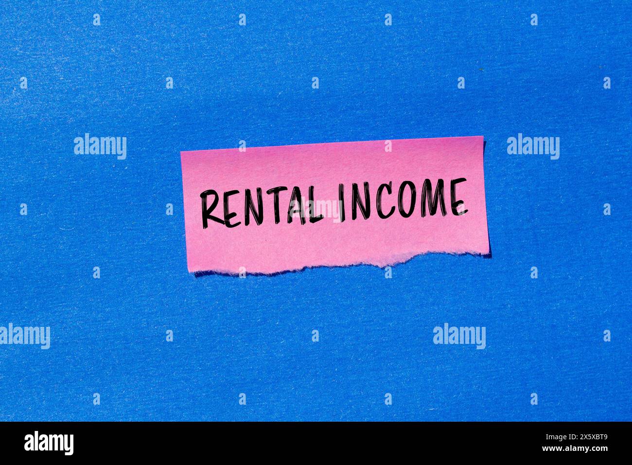 Rental income words written on ripped pink paper piece with blue ...
