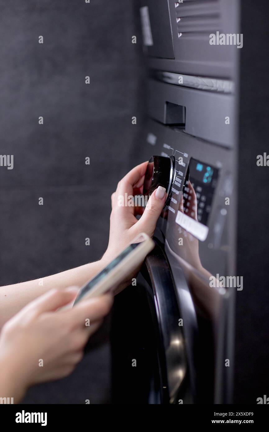 Woman controls washing machine with a phone Stock Photo - Alamy