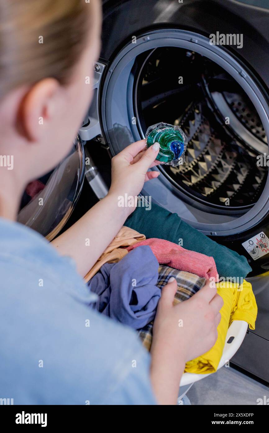 Woman putting laundry detergent capsule into washing machine indoors ...