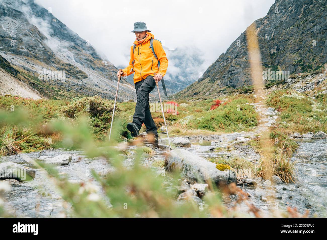 Man with backpack and trekking poles crossing mountain creek during ...