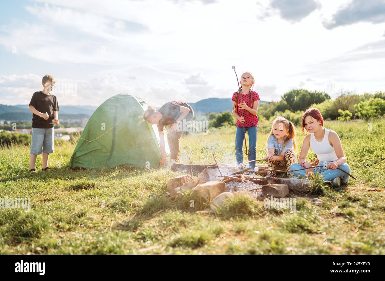 Three sisters cheerfully laughing and roasting marshmallows and candies ...