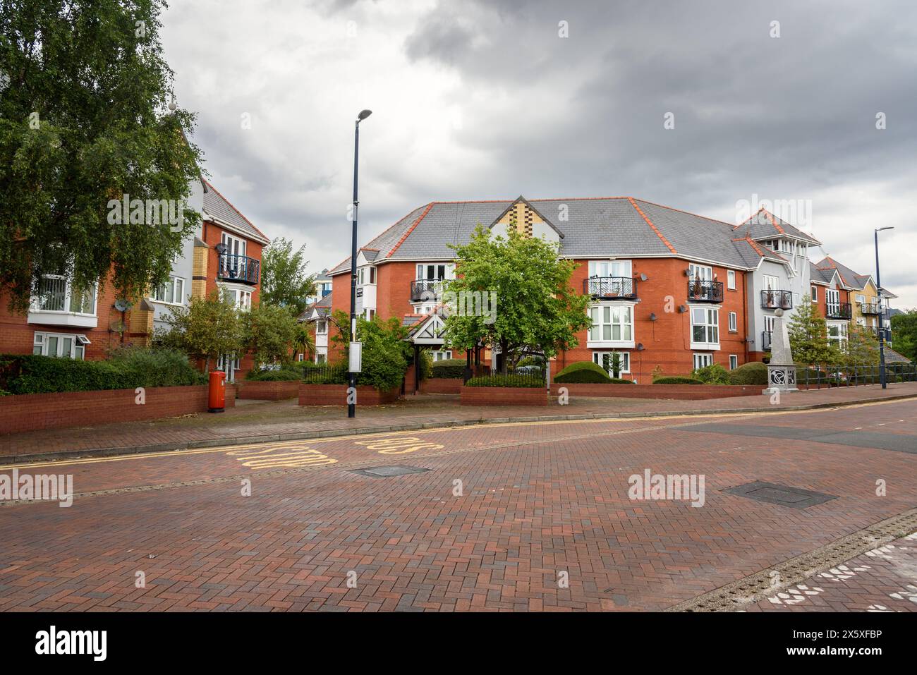 Apartment complex along a brick street on a cloudy day. A bus stop is ...