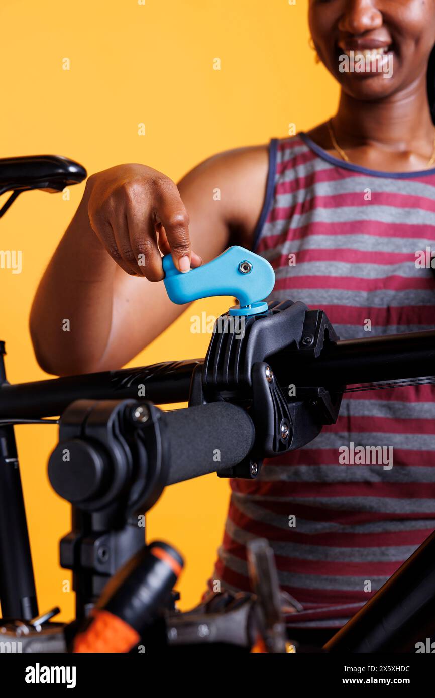 Black woman grips bicycle frame and securing it on repair stand against ...