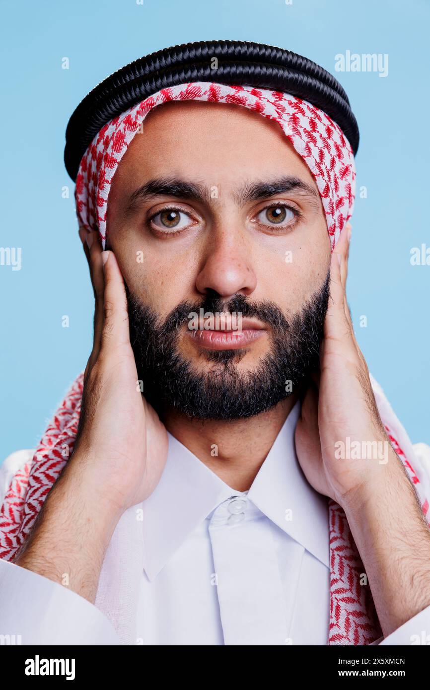 Man wearing muslim checkered headscarf covering ears with arms and ...