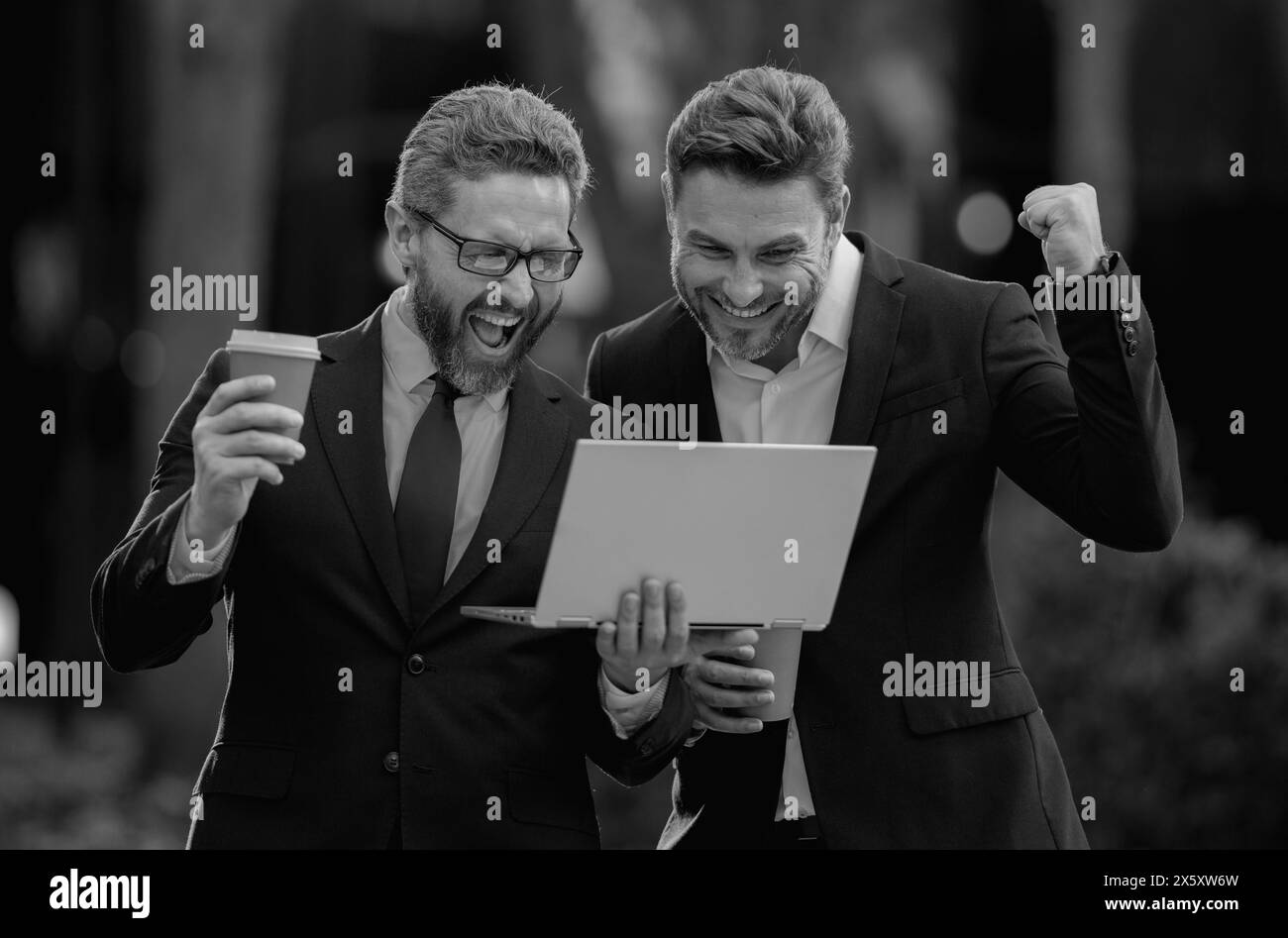 Two excited business man using laptop outdoor. Colleagues in suit ...
